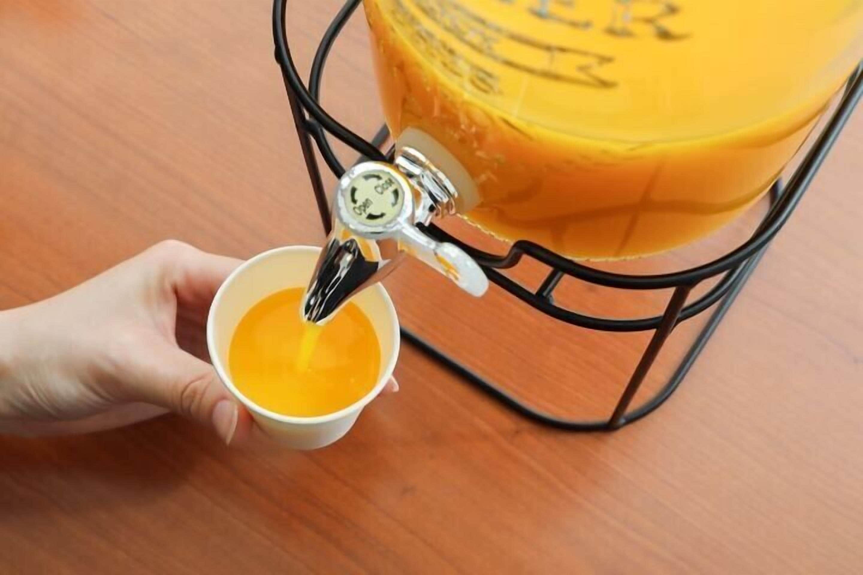 Uma mão despejando líquido laranja de um dispensador de metal em uma xícara branca.