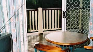 Uma área de pátio com uma mesa redonda e duas cadeiras, uma televisão e uma porta de correr de vidro que dá para um espaço exterior cercado.