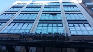 Um edifício moderno de hotel com vários andares, janelas amplas e um letreiro de 'Hotel' em destaque na parte inferior.