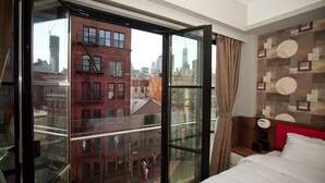Quarto de hotel com uma janela grande, uma cama, uma mesinha de cabeceira e uma parede com padrão geométrico.