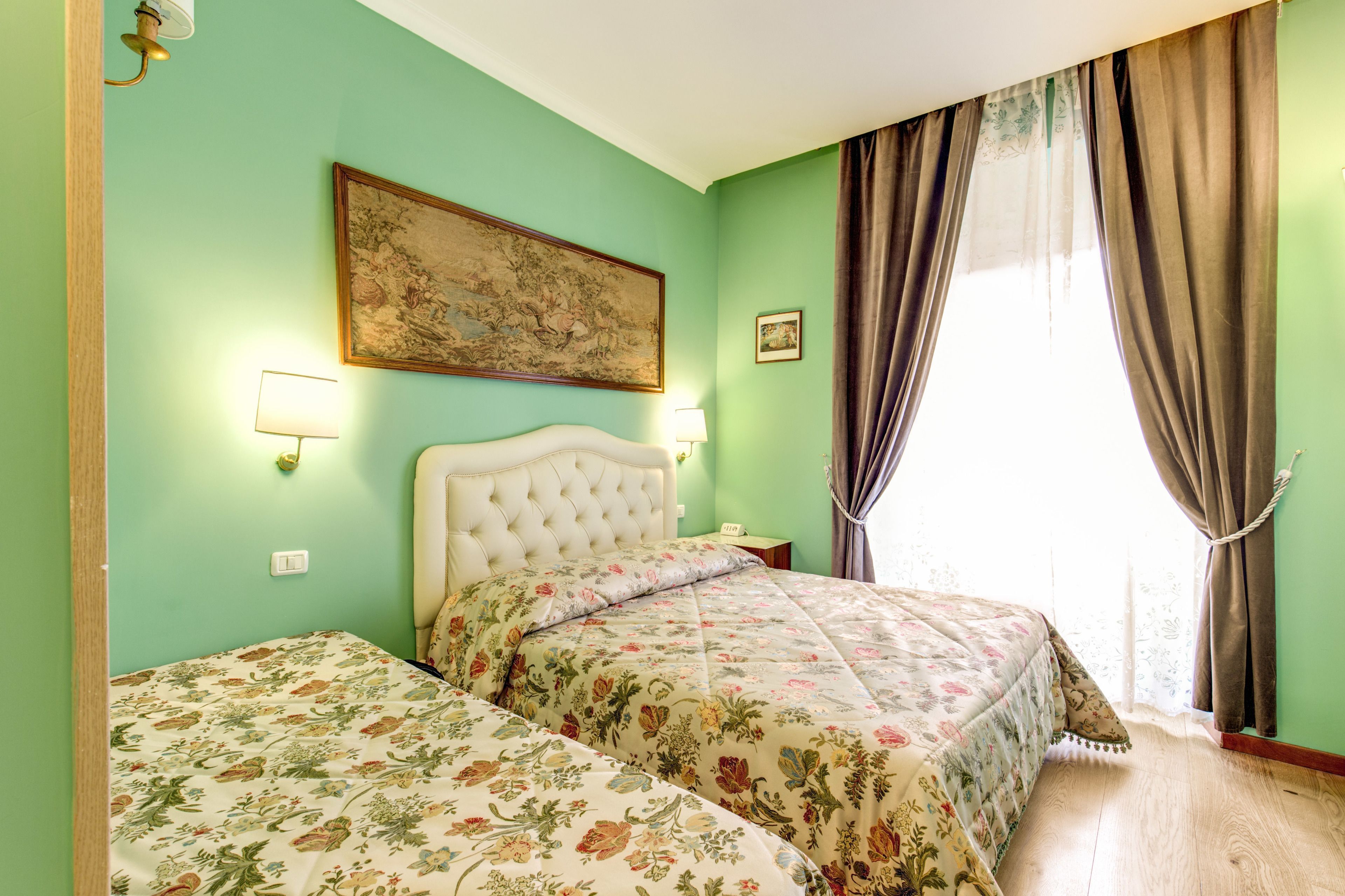 Quarto com uma cama, duas mesas de cabeceira, uma luminária na parede e uma janela com cortinas.