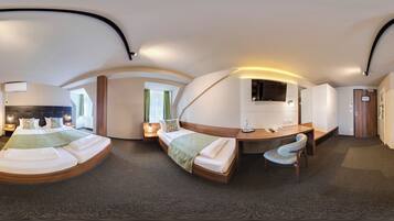 Quarto de hotel moderno com cama curva, escrivaninha, cadeira, televisão e porta do banheiro.