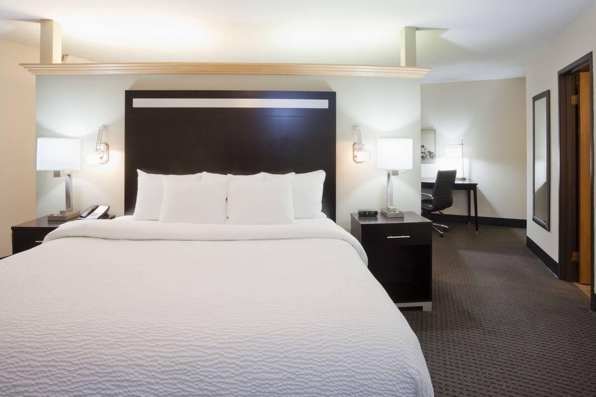 Quarto de hotel com uma cama grande, mesas de cabeceira com luminárias, uma escrivaninha e uma cadeira.