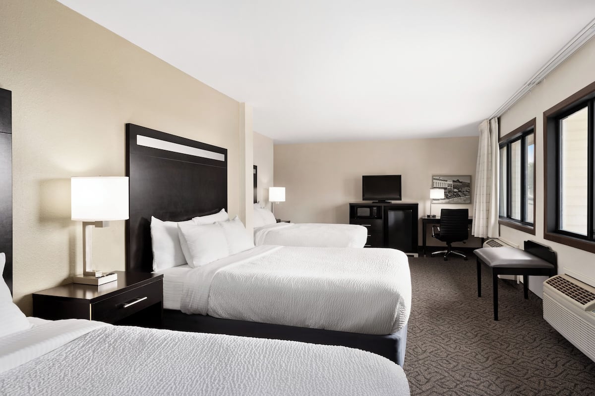 Quarto de hotel com duas camas, uma escrivaninha, uma cadeira, uma televisão e uma janela com cortinas.