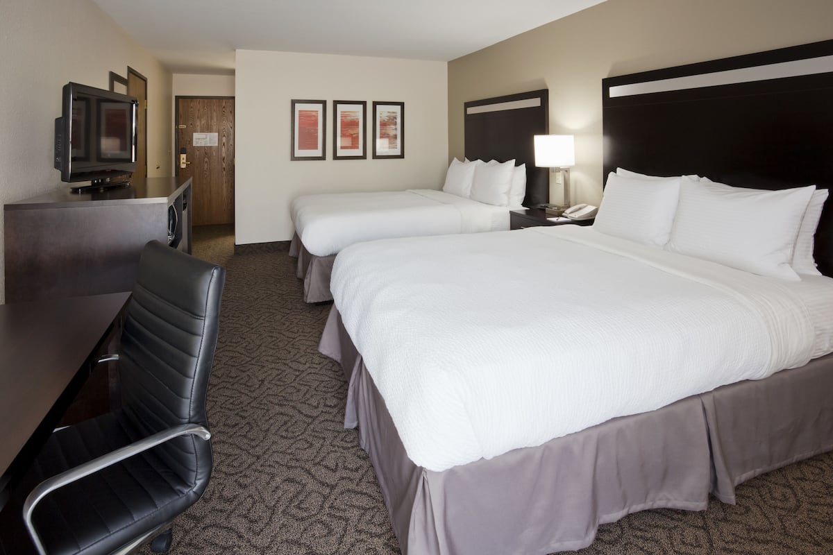 Quarto de hotel com duas camas, uma mesa, uma televisão e uma cadeira.