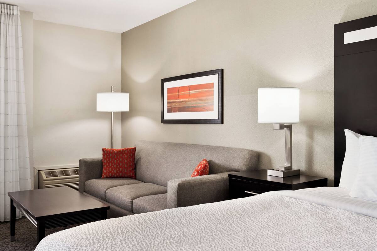 Quarto de hotel com uma cama, um sofá, uma mesa de trabalho e duas luminárias de cabeceira.