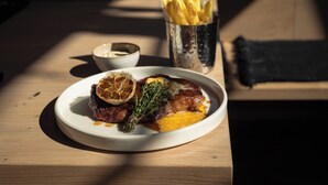 Um prato de comida com batatas fritas e uma pequena tigela de molho sobre uma mesa de madeira.