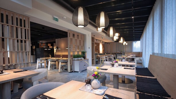 Um restaurante moderno com mobiliário de madeira, iluminação pendente e um layout limpo e organizado.