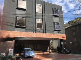 Um edifício com vários andares, entrada para estacionamento subterrâneo, placa BizHotel e um carro azul estacionado no interior.