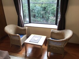 Quarto com duas cadeiras de vime, uma mesa pequena e janela com vista para o verde.