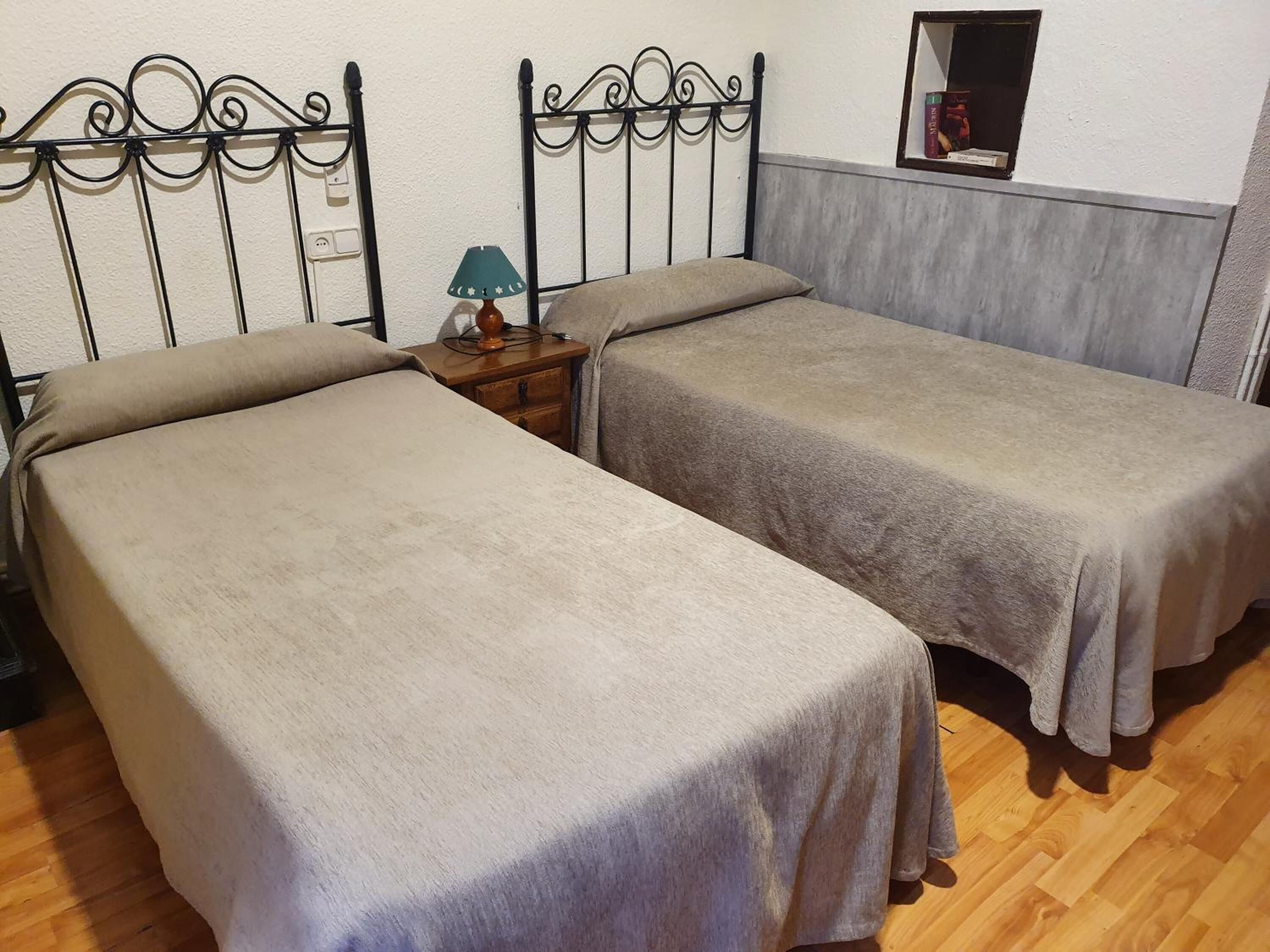 Quarto com duas camas de solteiro, uma mesa de cabeceira com abajur e um espelho na parede.