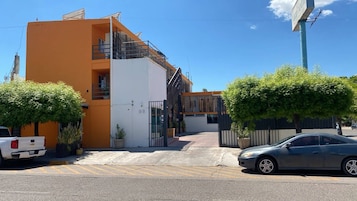Um edifício residencial com portão fechado, uma caminhonete estacionada e um carro na rua.