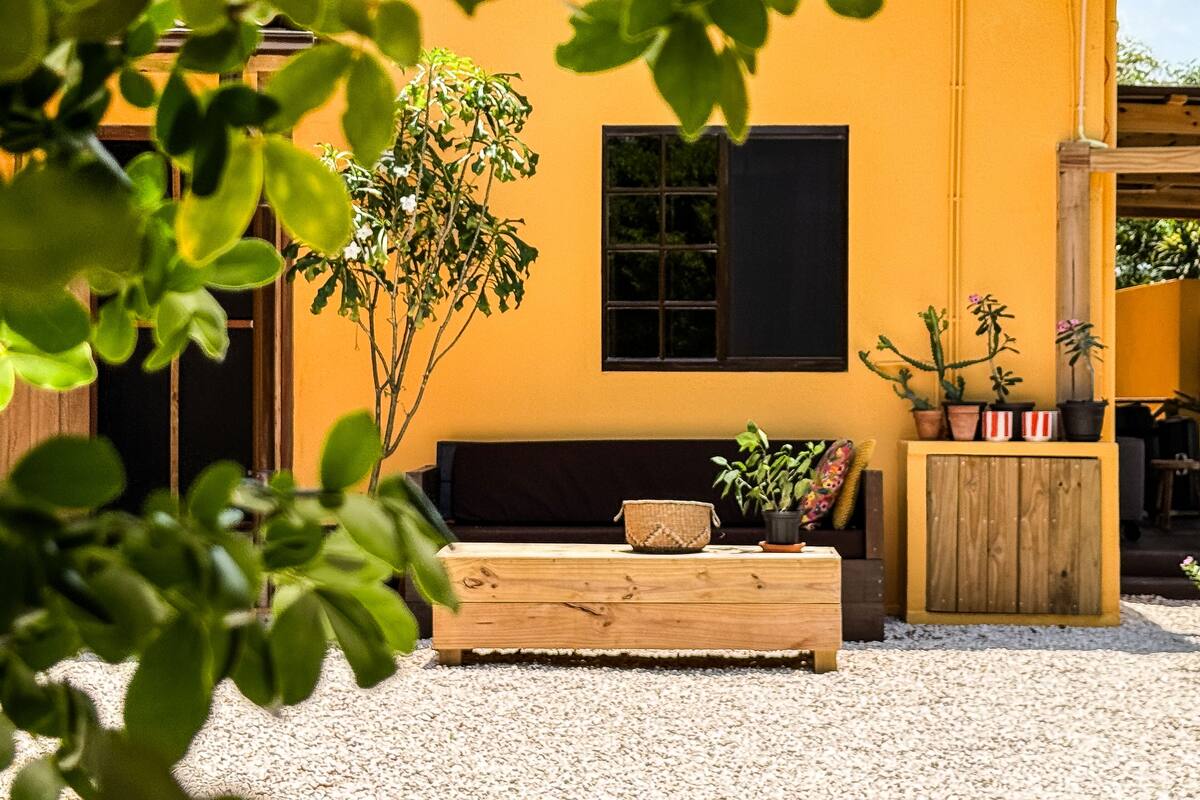 Uma área de estar ao ar livre aconchegante, com um banco de madeira, uma mesa pequena e plantas em vasos.
