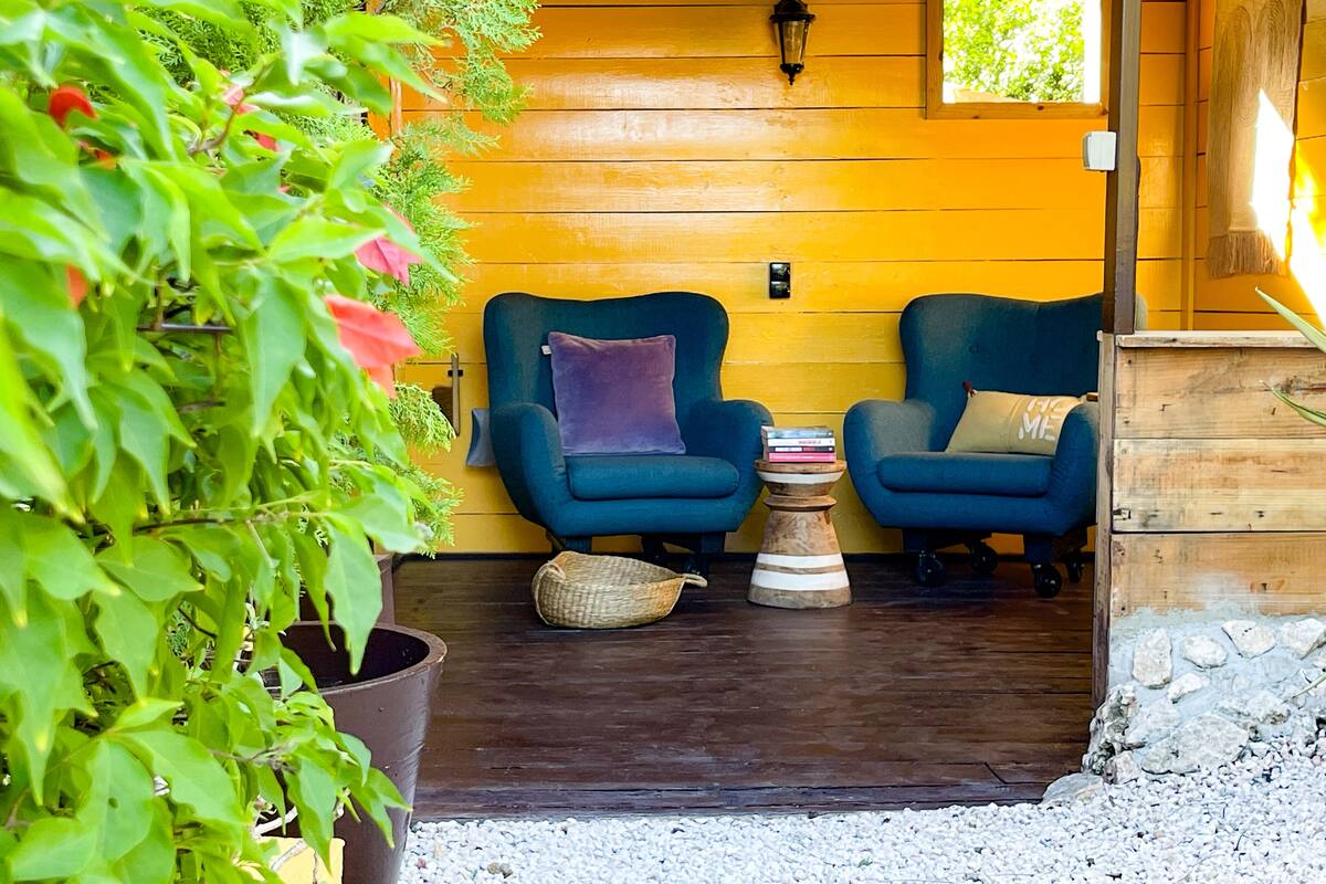 Uma cabana de madeira com duas poltronas azuis, uma mesinha com livros e um vaso de planta.