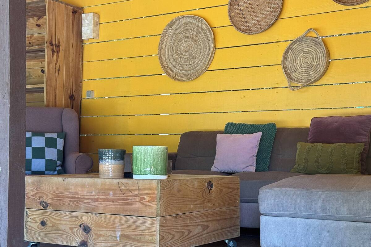 Uma sala de estar acolhedora com parede amarela, uma cômoda de madeira, um sofá cinza e uma poltrona marrom.