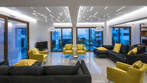 Uma sala de estar moderna com um sofá preto, poltronas amarelas e um sofá seccional preto. Há uma TV de tela plana e uma mesa de centro redonda.