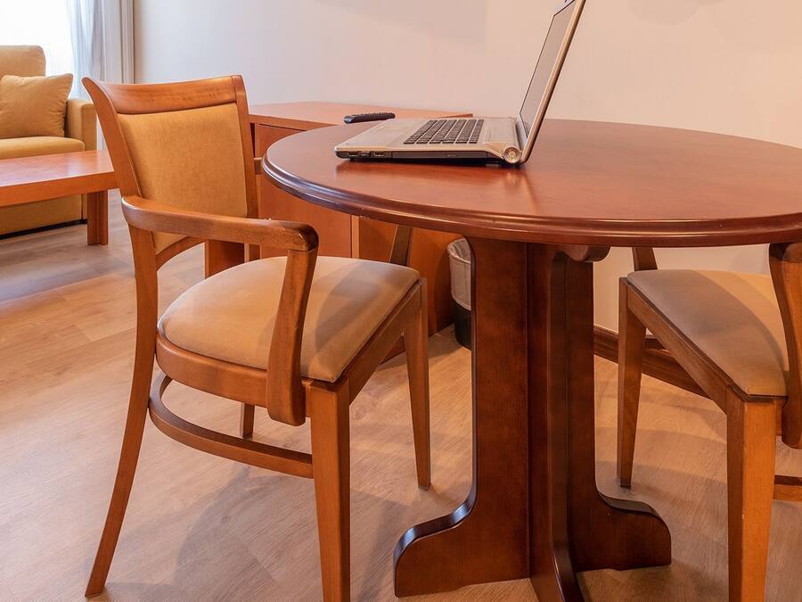 Uma sala de estar moderna com uma mesa de madeira redonda, duas cadeiras de madeira, um sofá e um laptop sobre a mesa.