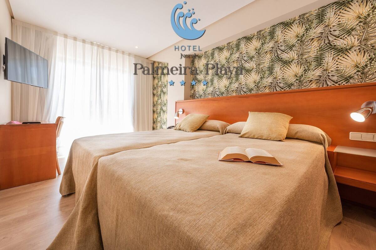 Quarto de hotel com duas camas, uma televisão e um papel de parede com padrão de folhagem tropical.