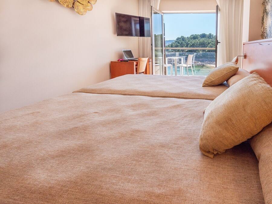 Quarto de hotel com uma cama grande, uma escrivaninha com um laptop e vista para o exterior através de uma porta de vidro.