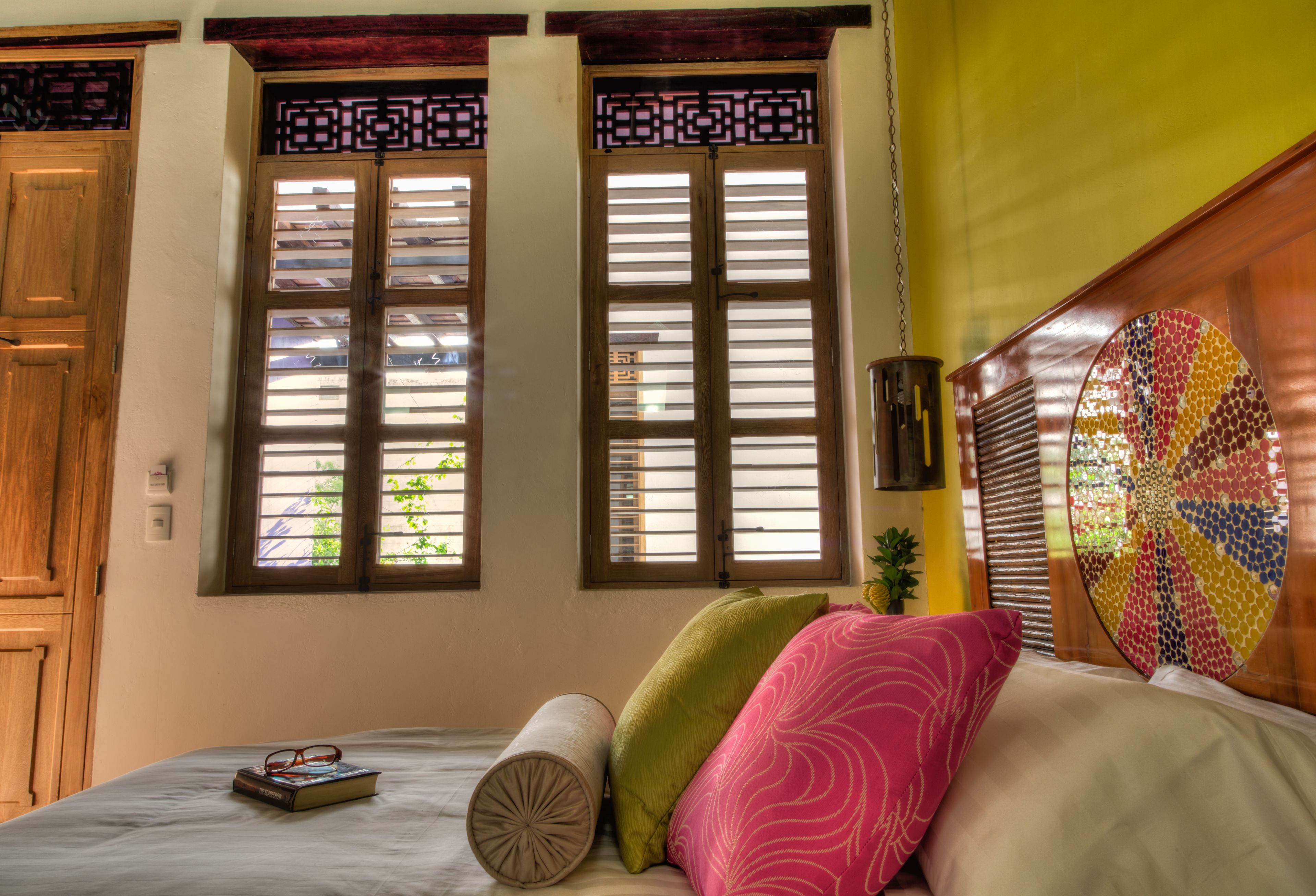 Um quarto com cama, janela com persianas, porta de madeira e um objeto decorativo na parede.