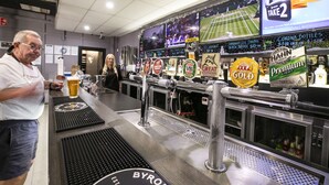 Espaço de bar com várias torneiras e uma tela grande exibindo eventos esportivos.