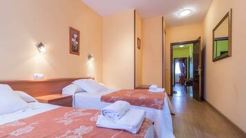 Quarto de hotel com duas camas, cada uma com colcha florida e toalha dobrada. Há luminárias na parede, um quadro e um espelho.