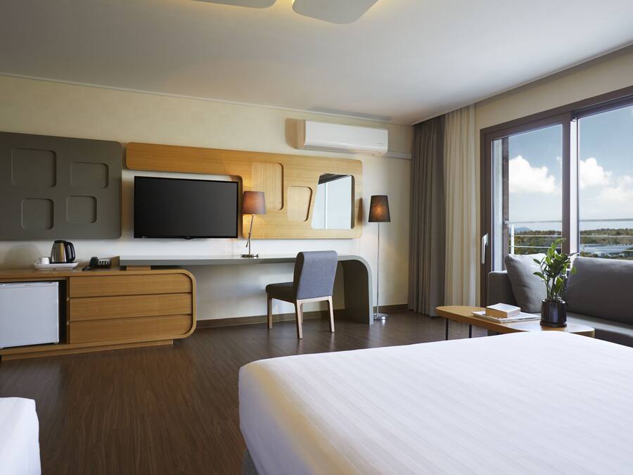 Quarto de hotel moderno com uma cama grande, escrivaninha com televisão de tela plana, mini-geladeira, cadeira e sofá.
