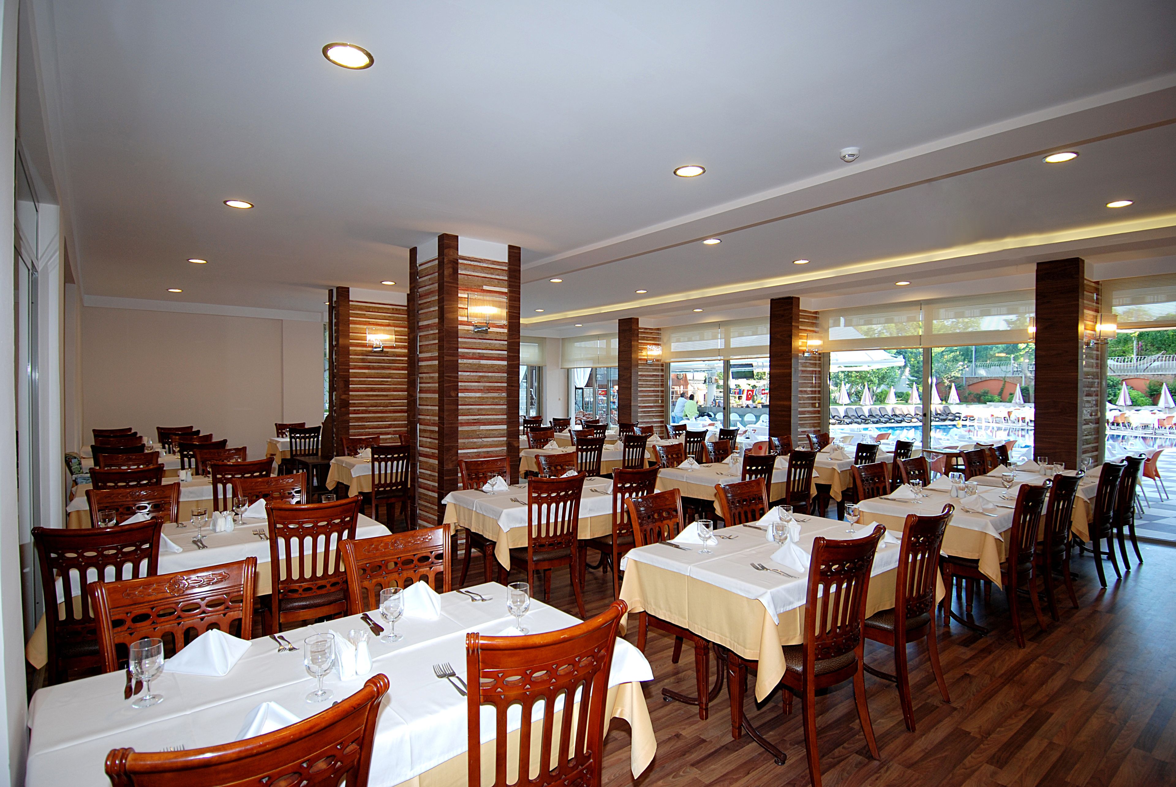 Restaurante com várias mesas e cadeiras, grandes janelas e vista para uma área de piscina.