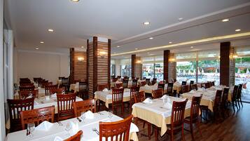 Restaurante com várias mesas e cadeiras, grandes janelas e vista para uma área de piscina.