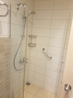 Um chuveiro com porta de vidro, um chuveiro manual, um chuveiro fixado na parede e uma prateleira no canto.