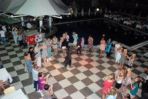 Piso xadrez com pessoas reunidas, área de bar com balcão vermelho e mesas com guarda-sóis.
