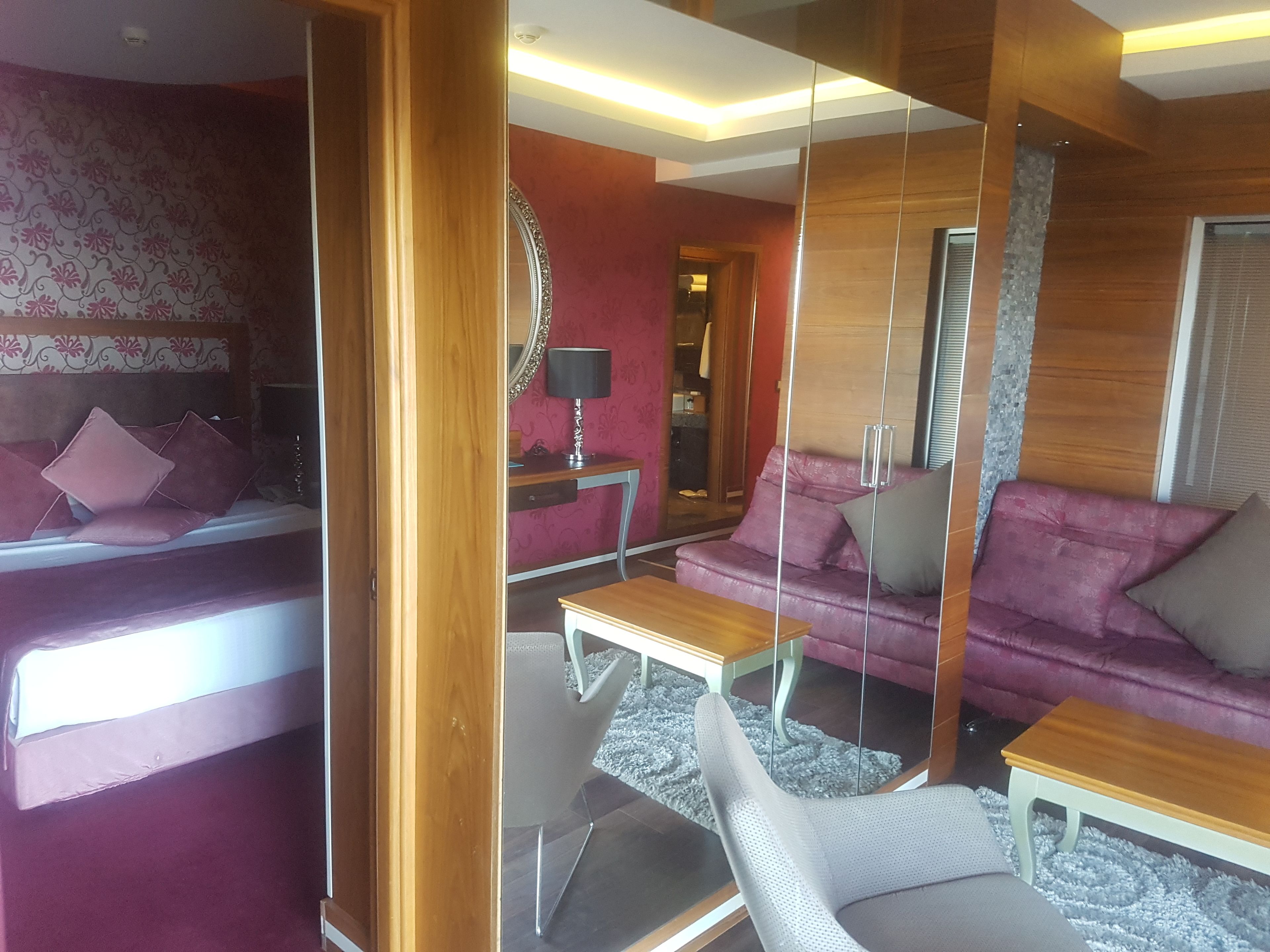Quarto de hotel moderno com uma cama, um sofá, uma mesa pequena e um espelho.