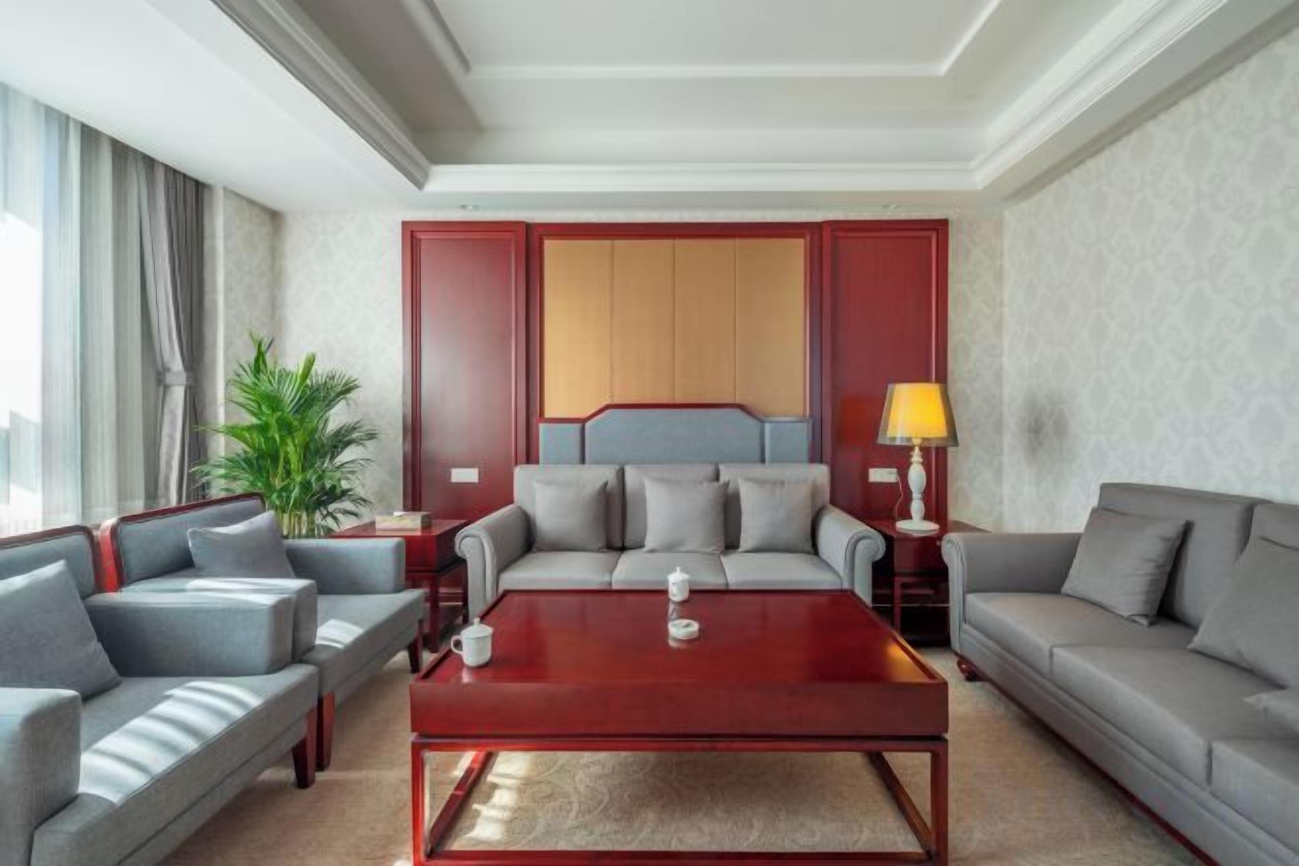 Quarto de hotel moderno com um amplo sofá, uma mesa de centro e cabeceira decorativa.