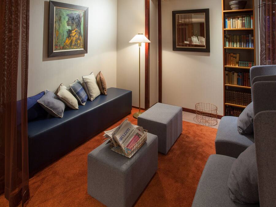 Um espaço aconchegante para leitura, com um sofá, pufes e uma estante de livros.