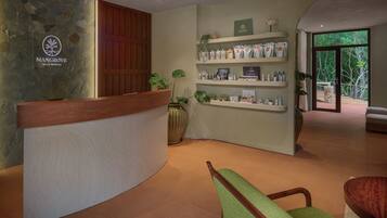 Uma área de recepção com parede de pedra, balcão de madeira e prateleiras com produtos de spa.
