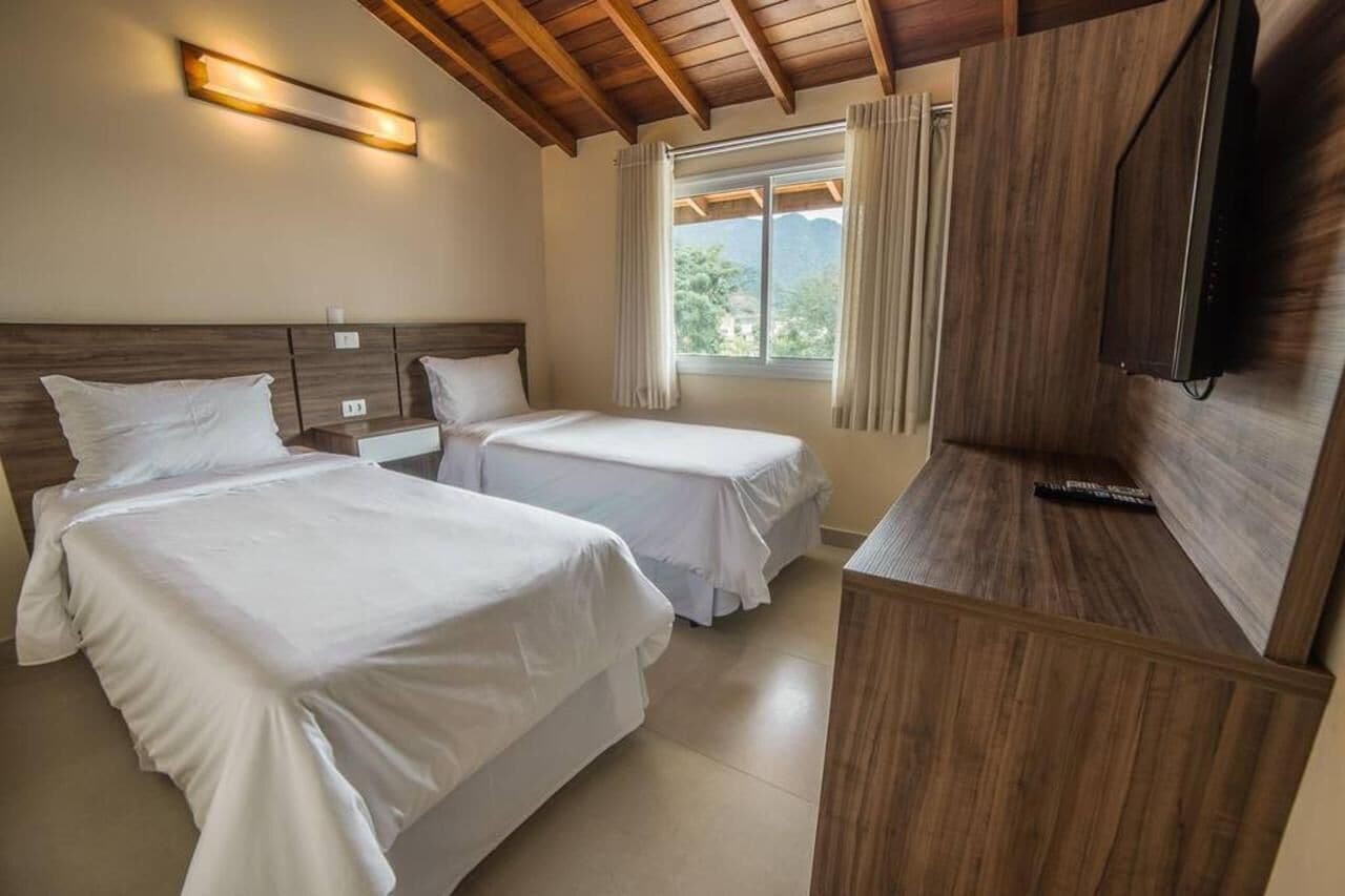 Quarto com duas camas, teto de madeira, televisão na parede e janela com cortinas.