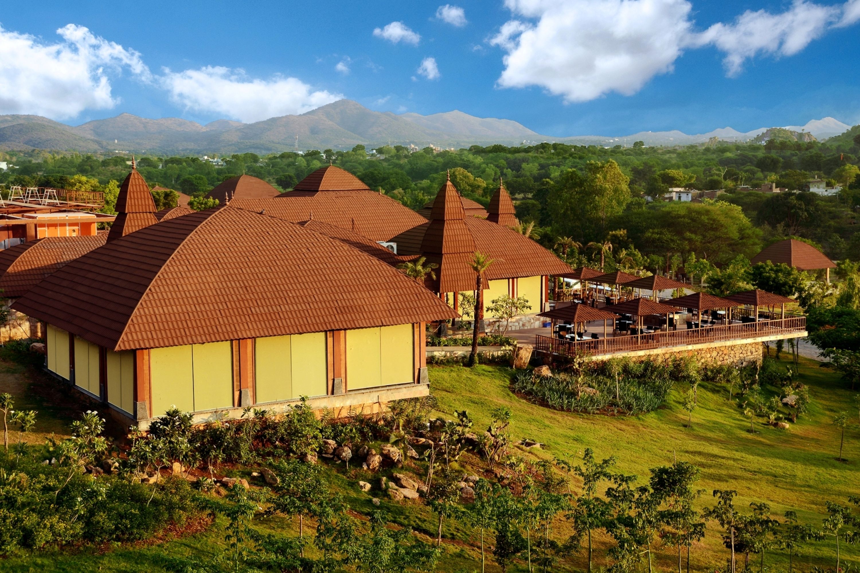 Um resort com vários edifícios com telhados vermelhos, cercado por vegetação exuberante e montanhas ao fundo.