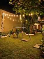 Área externa bem iluminada com balanço, luzes de festa e um jardim com diversas plantas.