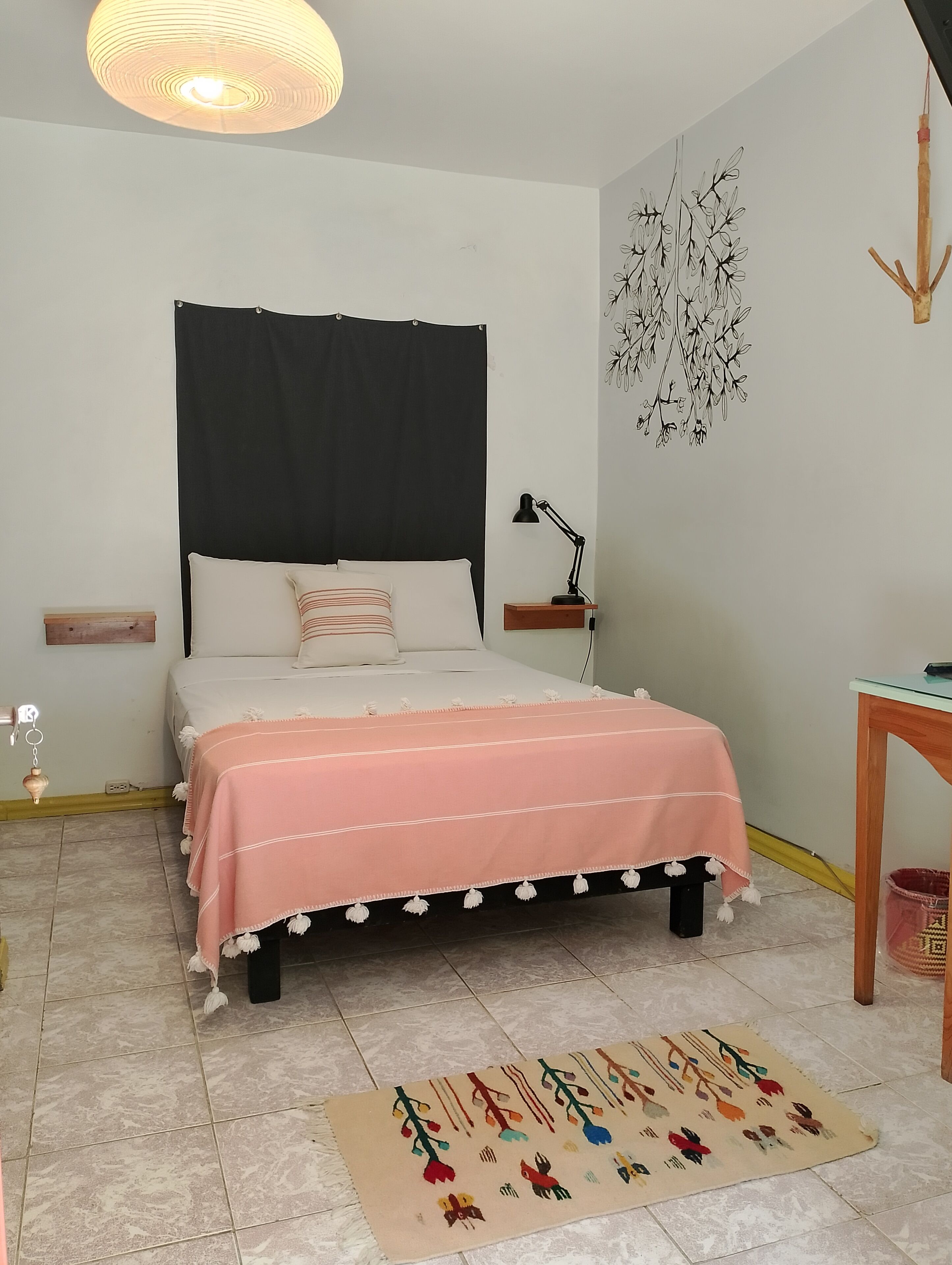 Quarto com cama, escrivaninha, luminária, obra de arte na parede e tapete.