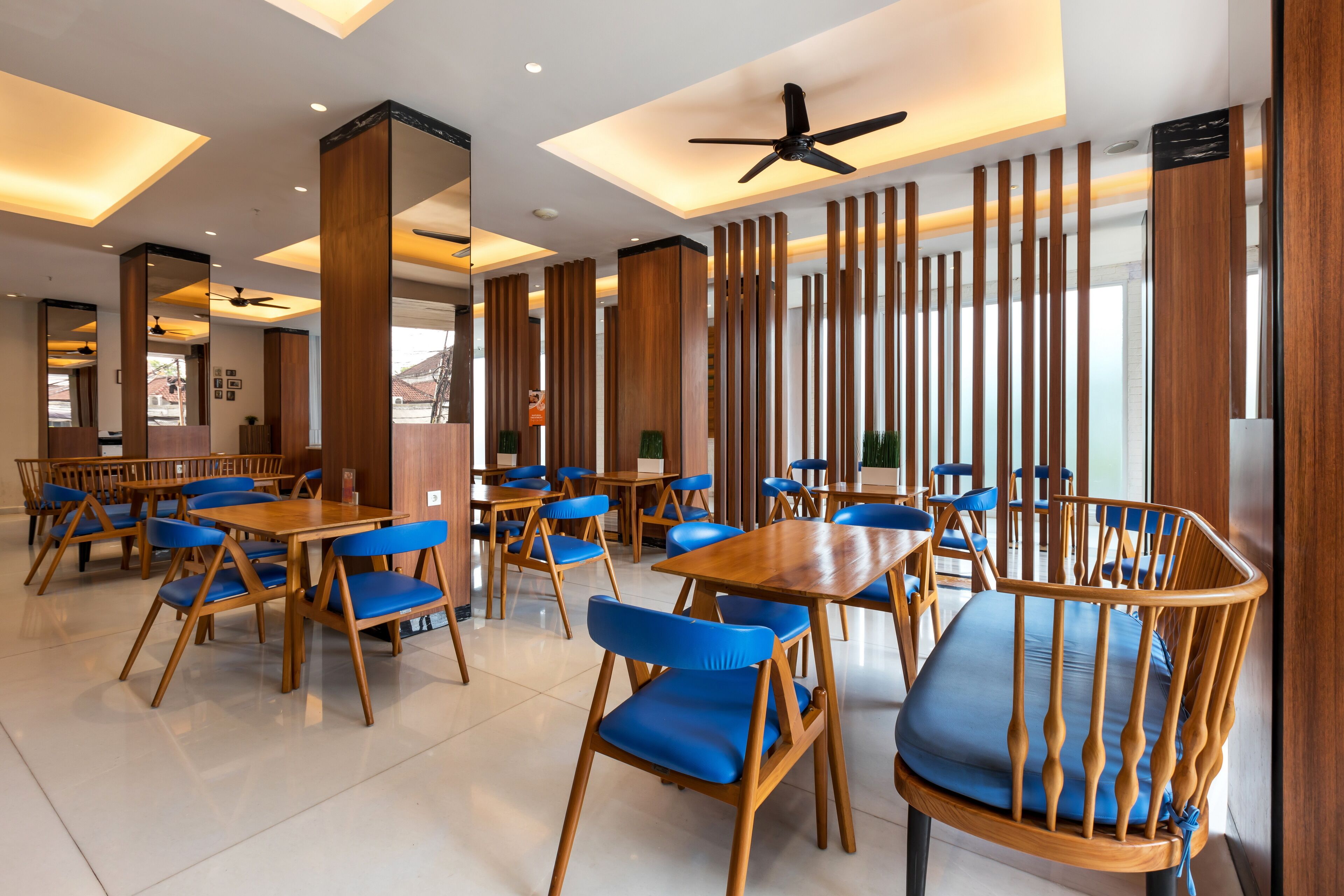 Uma sala de jantar moderna com mesas de madeira e cadeiras azuis, com ventoinhas de teto e iluminação embutida.