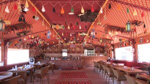 Um restaurante com teto estampado em vermelho, decorações pendentes e um bar central. Mesas e cadeiras dispostas para refeições.