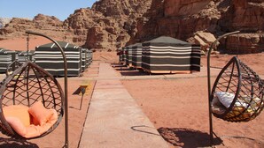Acampamento no deserto com cadeiras suspensas e tendas listradas.