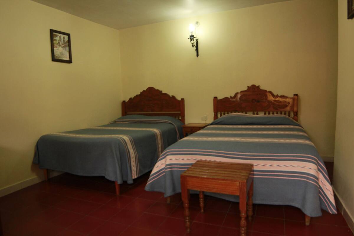 Quarto com duas camas de solteiro, uma mesa de cabeceira de madeira e uma pequena mesa.