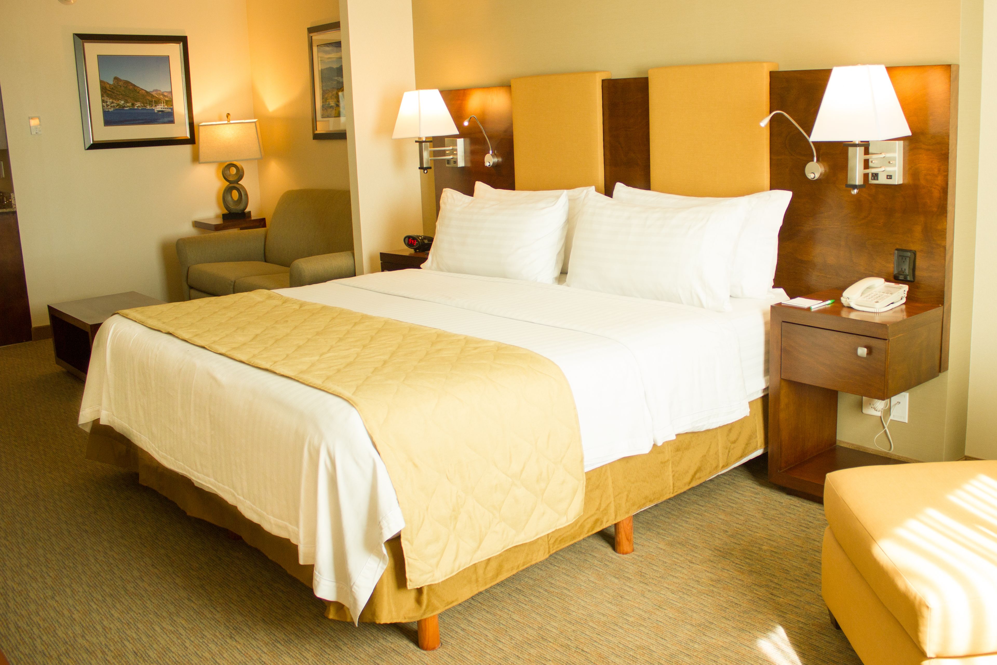 Quarto de hotel com uma cama grande, duas mesas de cabeceira, uma cadeira e um abajur.