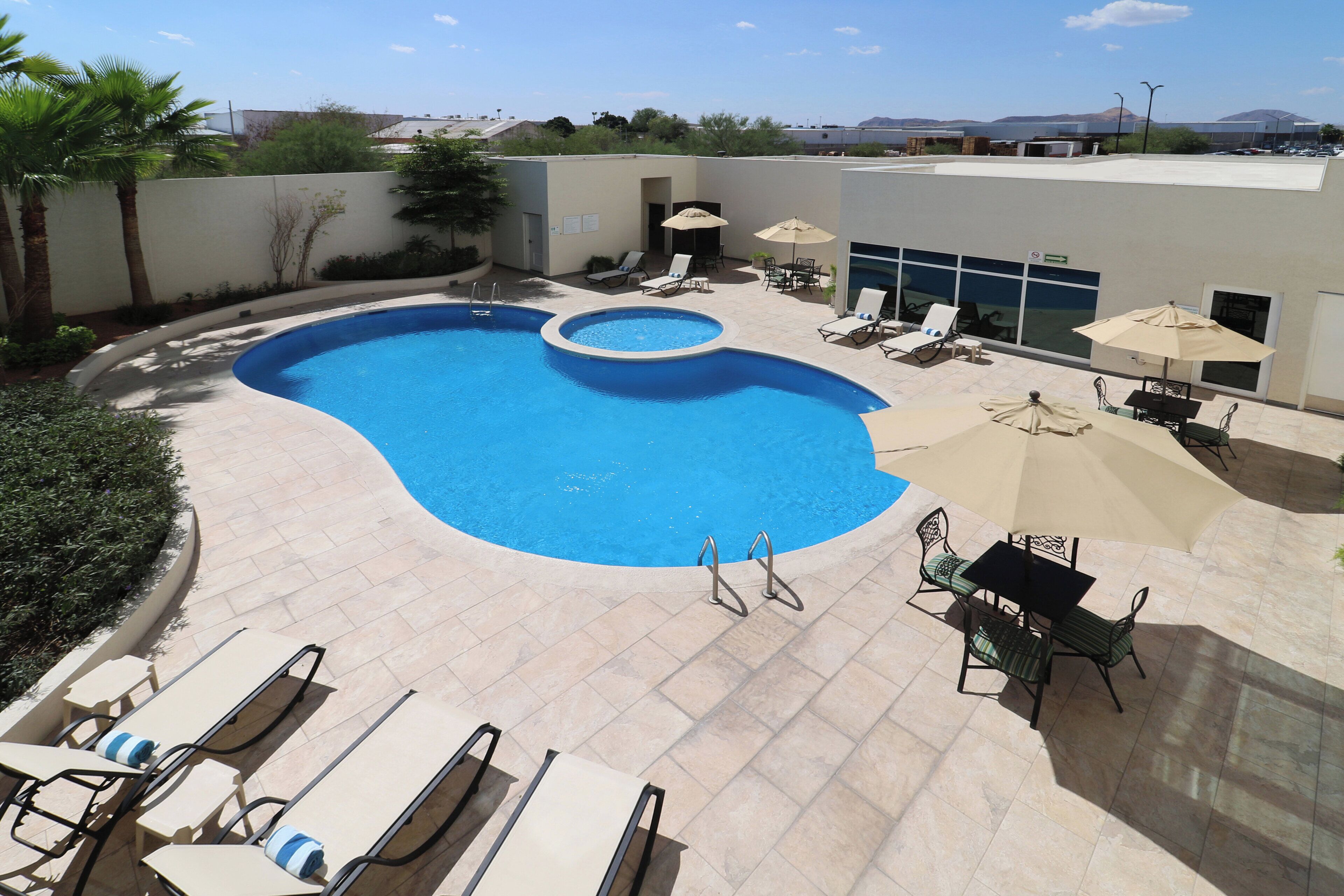 Piscina com espreguiçadeiras e guarda-sóis, cercada por um espaço de lazer com piso cerâmico.
