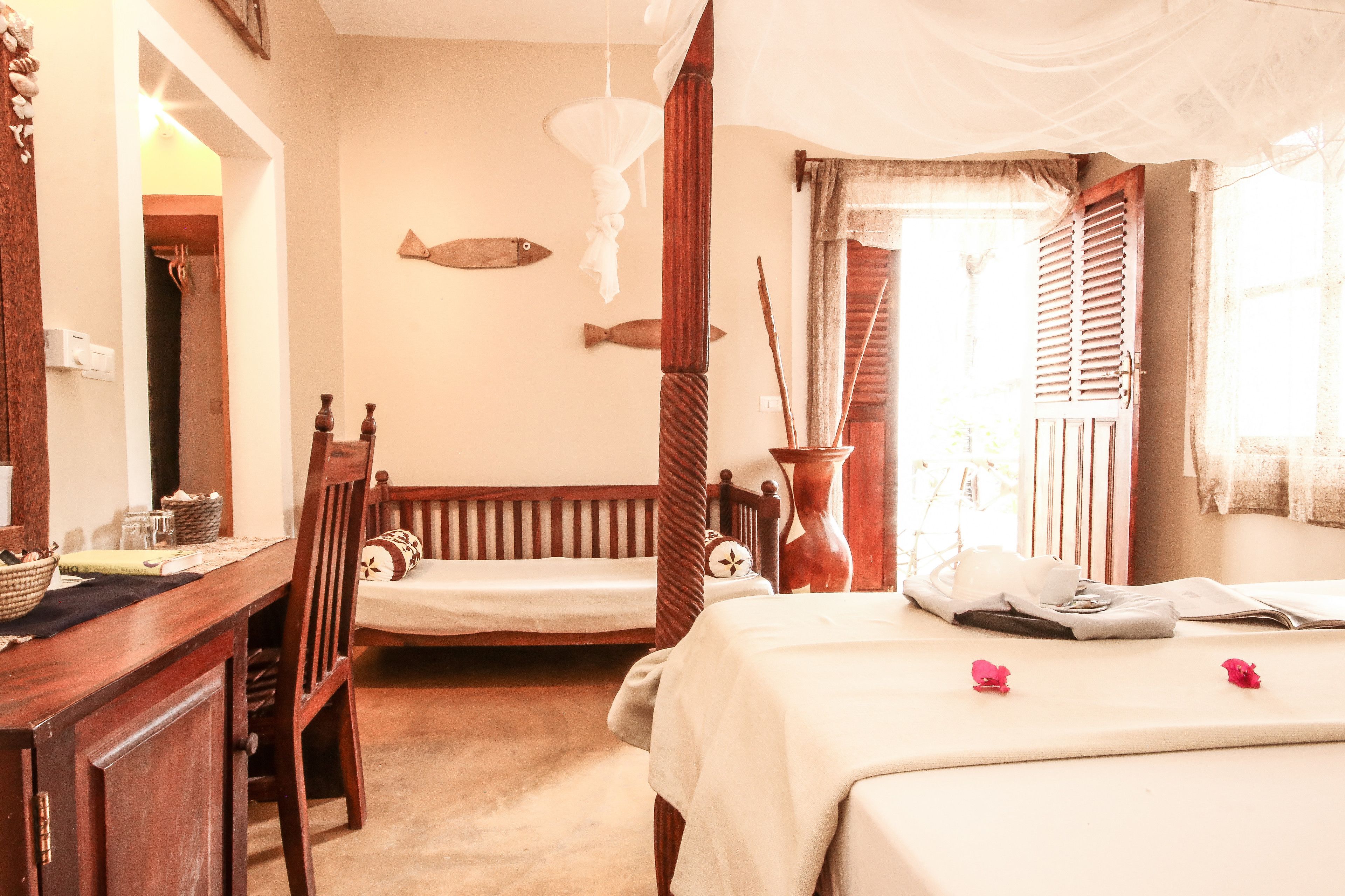 Quarto com cama de dossel, escrivaninha de madeira, cadeira, mesa de cabeceira e decoração de peixe na parede.