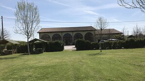 Um edifício com telhado ladrilhado e janelas em arco, rodeado por um jardim bem cuidado e árvores.