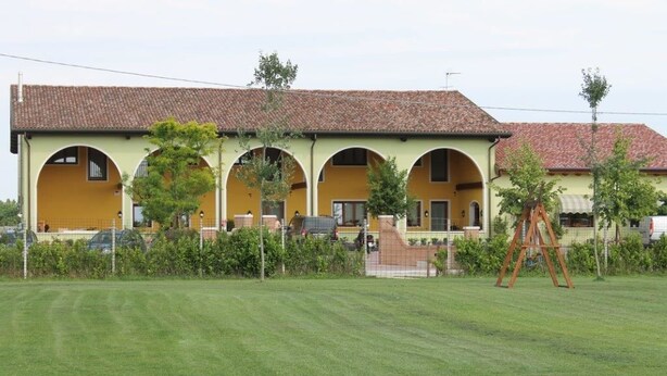 Um edifício com fachada amarela e telhado de telhas vermelhas, apresentando diversas janelas em arco e um gramado na frente.