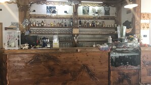 Uma área de bar com decoração em madeira, prateleiras com garrafas, copos e um balcão com uma máquina registradora.