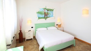 Um quarto com uma cama, uma mesa de cabeceira, um abajur, um vaso com galhos e um quadro na parede.